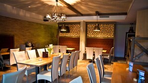 Uma área de refeições moderna, com mesas de madeira, cadeiras brancas, um candelabro e uma parede decorativa com padrões circulares.