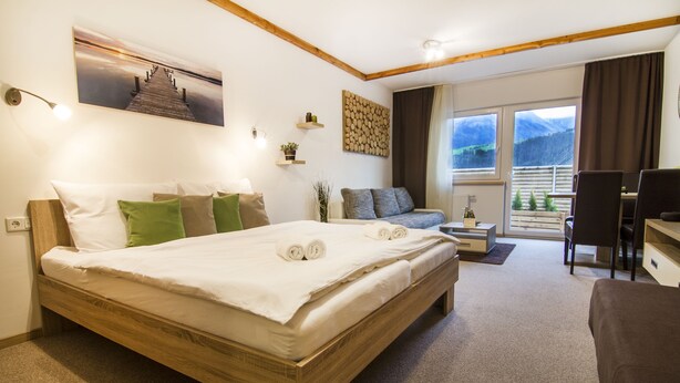 Quarto de hotel com uma cama grande, um sofá, uma escrivaninha e vista para montanhas pela janela.