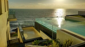 Uma piscina infinita moderna com vista clara para o oceano e o sol se pondo ao fundo.