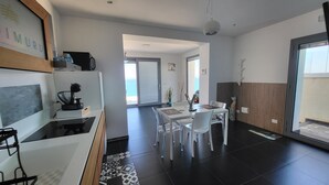 Cozinha moderna com cafeteira, área de refeições com mesa e cadeiras, e vista para o exterior.