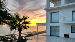 Um edifício moderno com piso xadrez, uma palmeira e vista para o oceano ao pôr do sol.