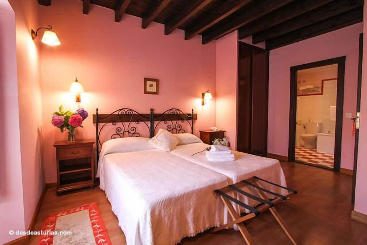 Quarto com cama de casal, mesas de cabeceira, uma cadeira de madeira e banheiro visível por uma porta aberta.