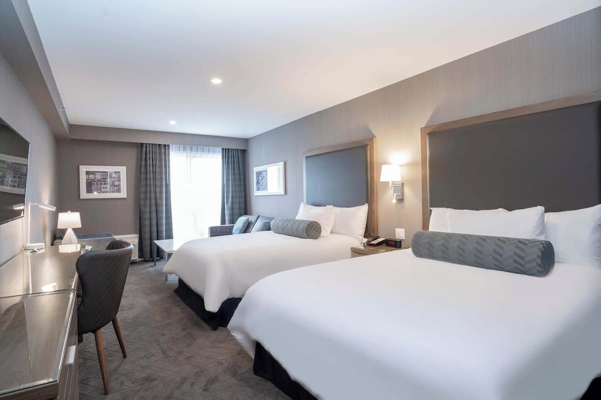 Quarto de hotel com duas camas, uma mesa, uma cadeira e uma televisão.
