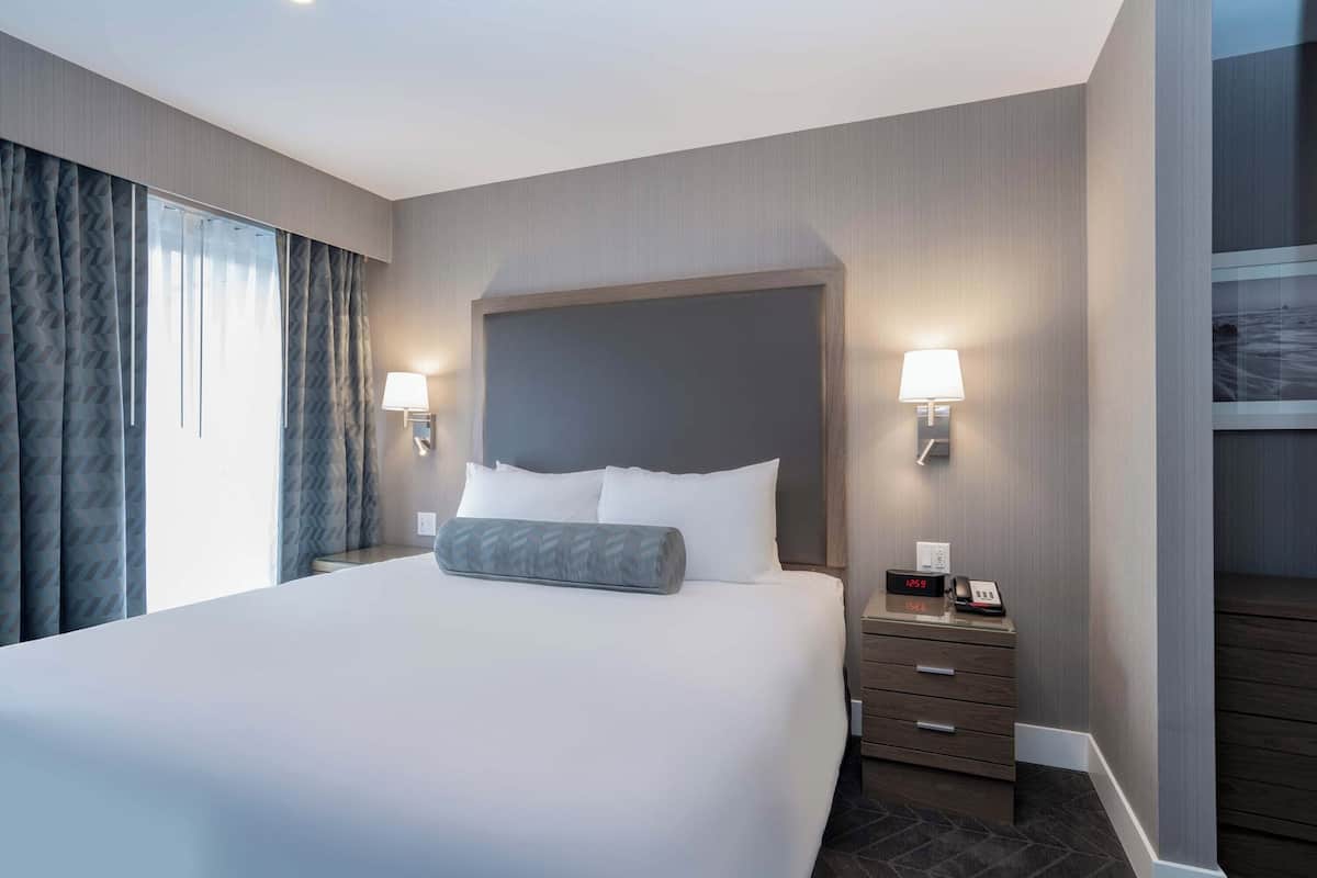Quarto de hotel com uma cama grande, duas luminárias de cabeceira, mesa de apoio com telefone e vista para o exterior pela janela.