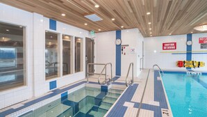Uma piscina interior com água cristalina, paredes revestidas de azulejos e teto de madeira.