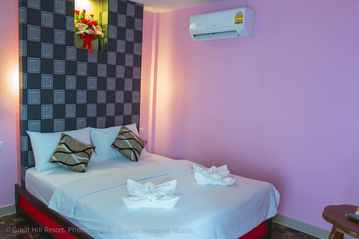 Quarto de hotel com cama, almofadas, ar condicionado fixado na parede e uma mesinha.