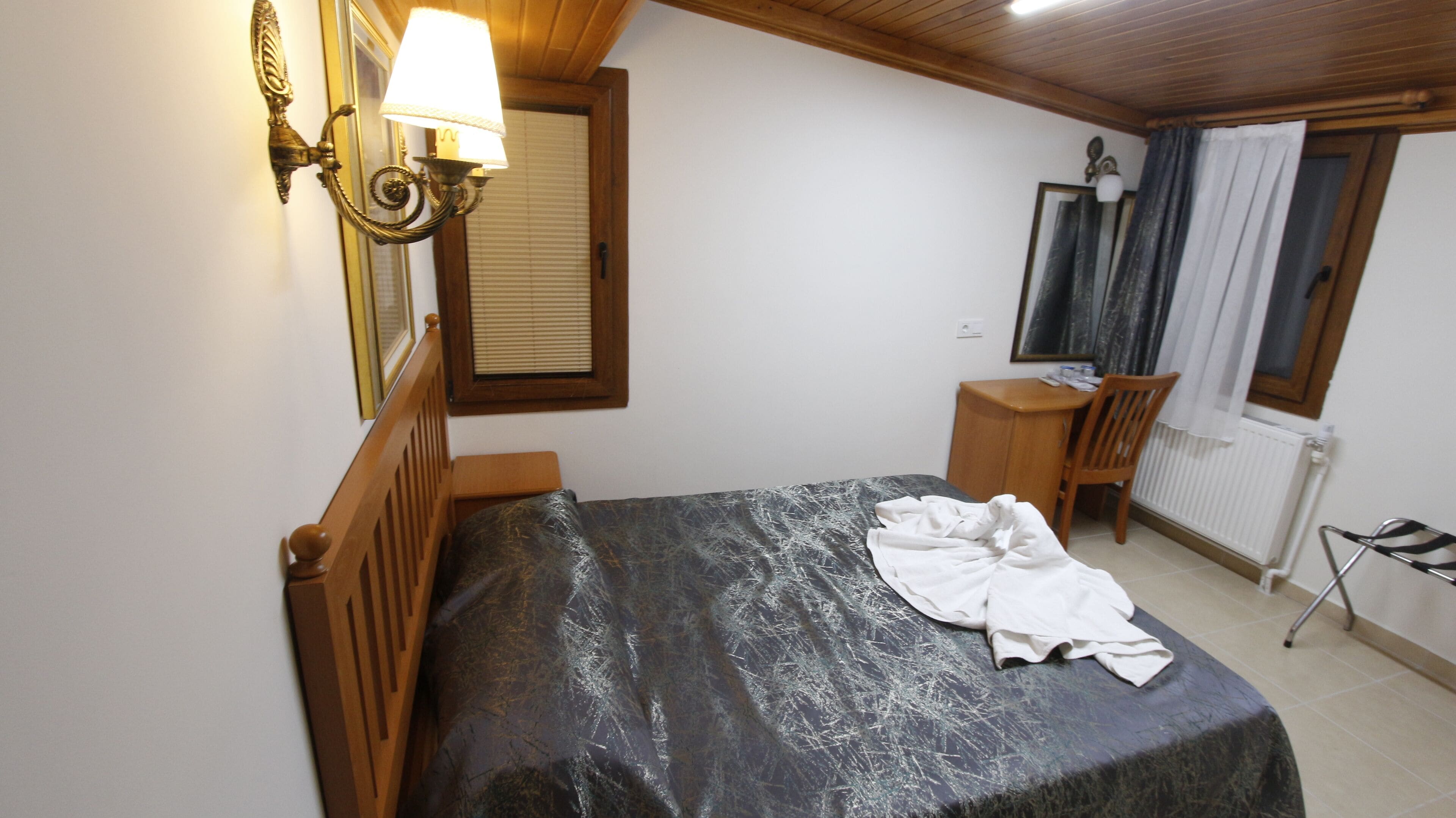 Um quarto com cama de madeira, uma escrivaninha, uma cadeira e um radiador.