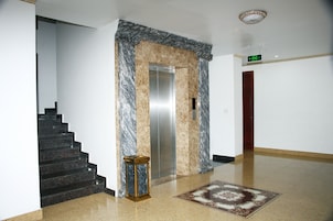 Um hall com elevador de mármore, um banco de madeira e um tapete estampado.