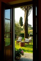 Uma porta aberta dá para um jardim com móveis de vime e uma grande árvore.