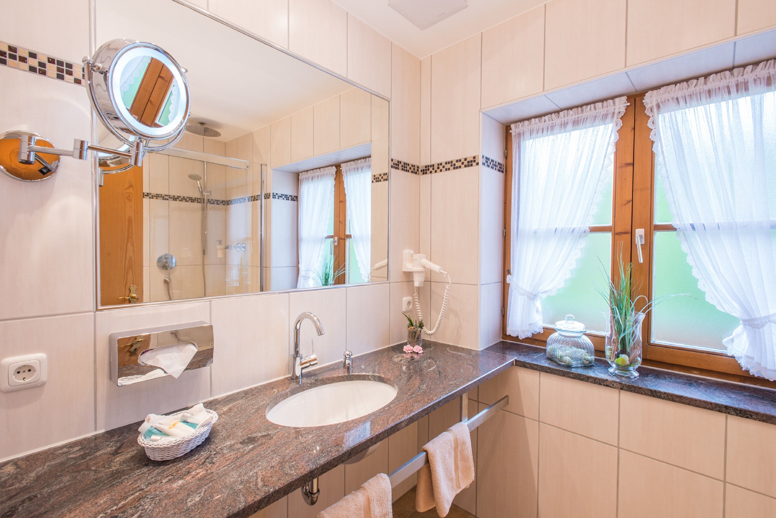 Um banheiro com pia de mármore, espelho, porta-toalhas e janela com cortinas.