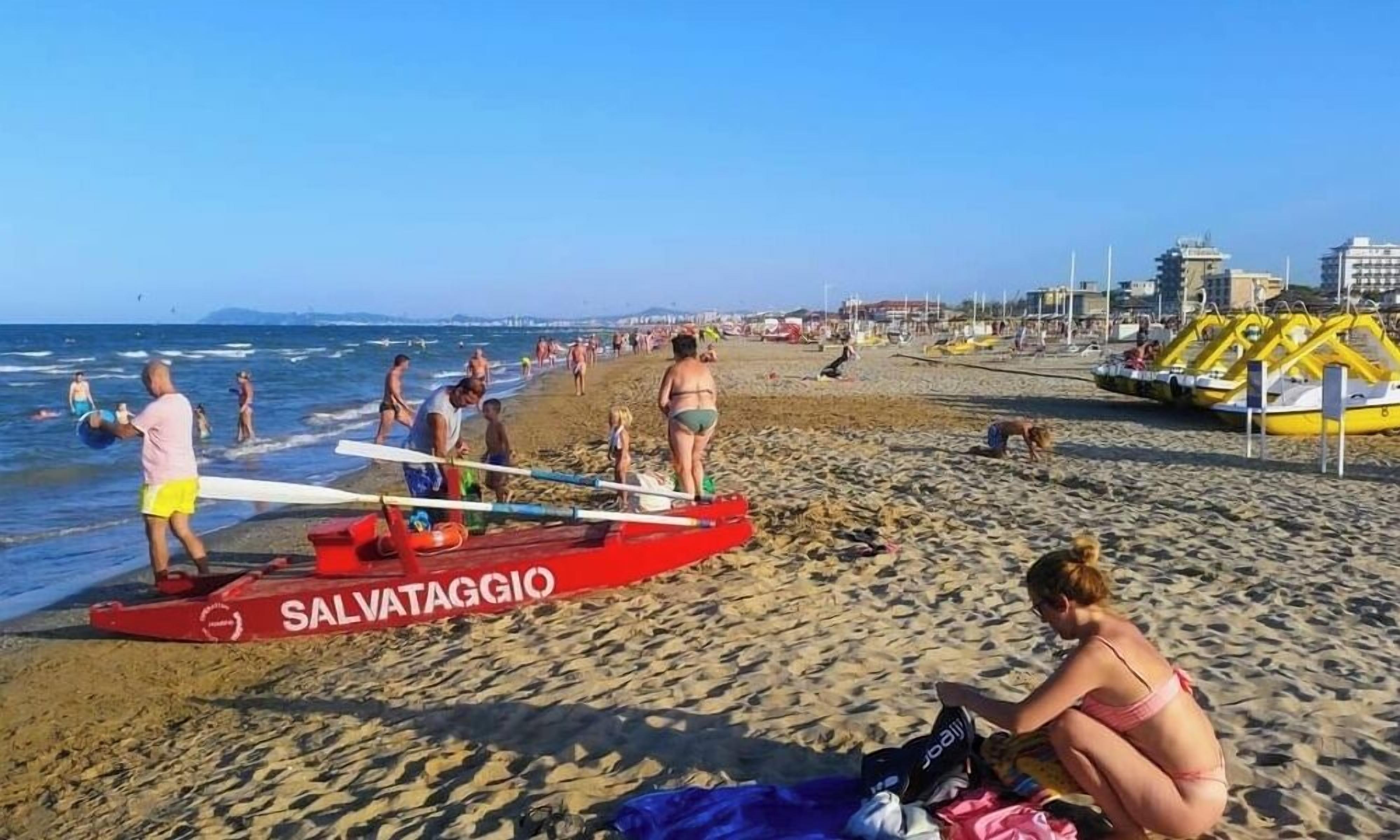 Uma praia com pessoas, barcos e uma torre salva-vidas.