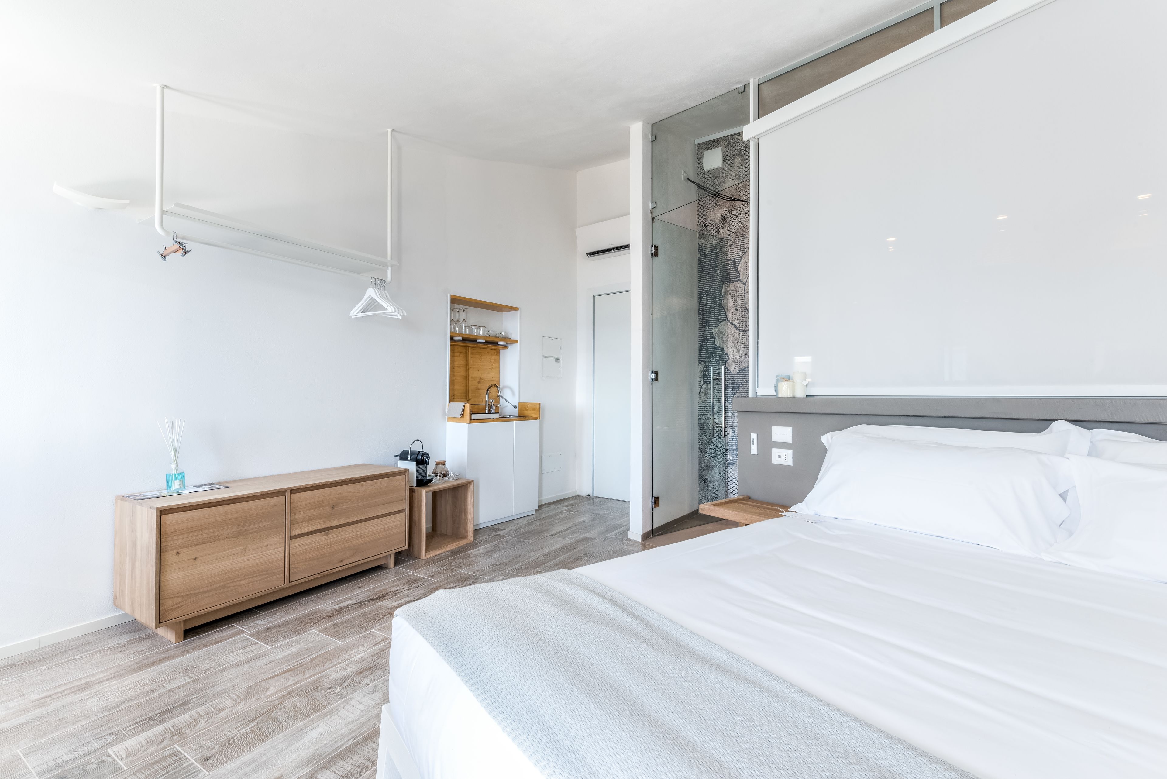 Quarto moderno com uma cama grande, cômoda de madeira, escrivaninha pequena e box de vidro.