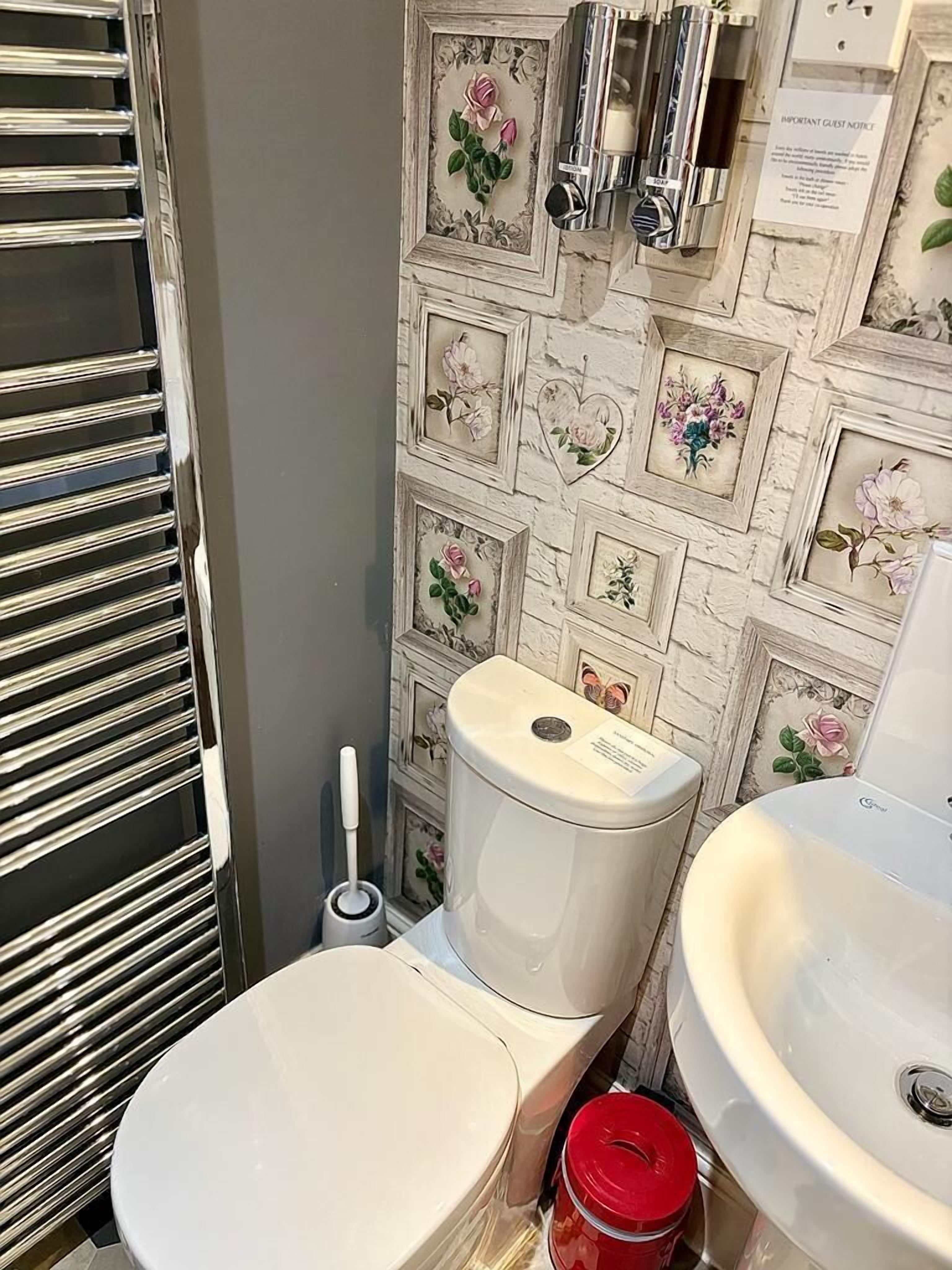 Casa de banho com sanita, bidé e lavatório, destacando uma parede de azulejos decorativa com motivos florais.