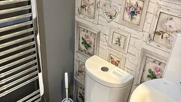 Casa de banho com sanita, bidé e lavatório, destacando uma parede de azulejos decorativa com motivos florais.