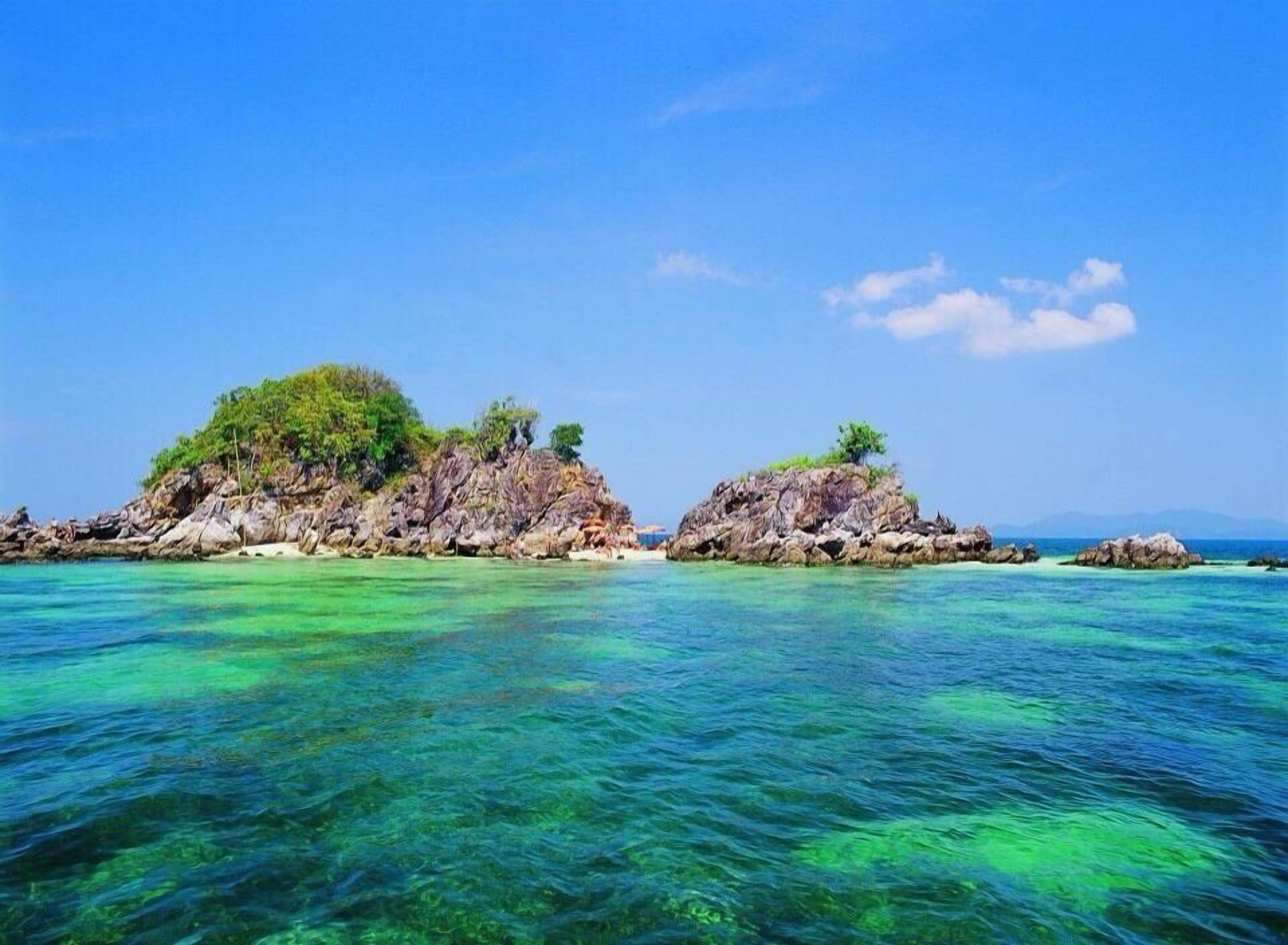 Visão nítida de uma ilha tropical com terreno rochoso e vegetação exuberante, banhada por águas azul-turquesa.