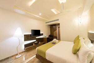 Quarto de hotel com cama, televisão, escrivaninha e abajur.