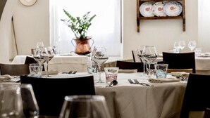 Uma área de refeições com mesas postas, um candelabro e uma estante com pratos.