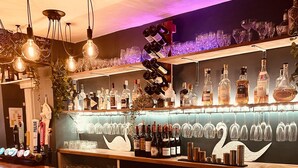 Uma área de bar com balcão de madeira, copos de vinho pendurados e prateleiras repletas de garrafas.