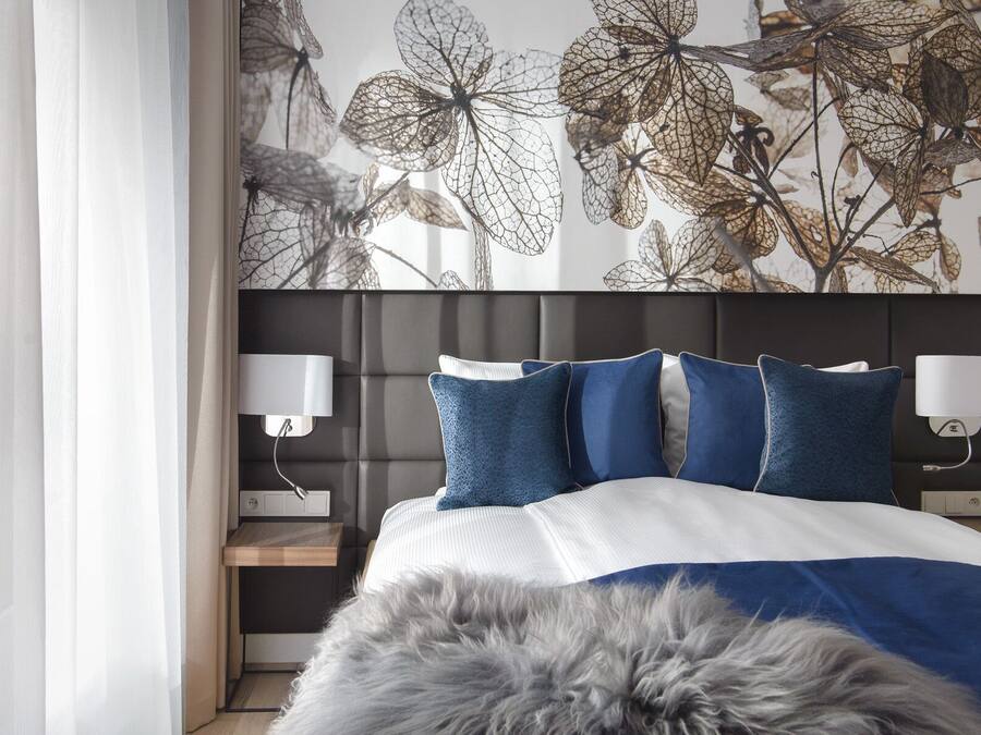 Quarto moderno com uma cama grande, duas luminárias de cabeceira e uma parede com padrão de folhas.