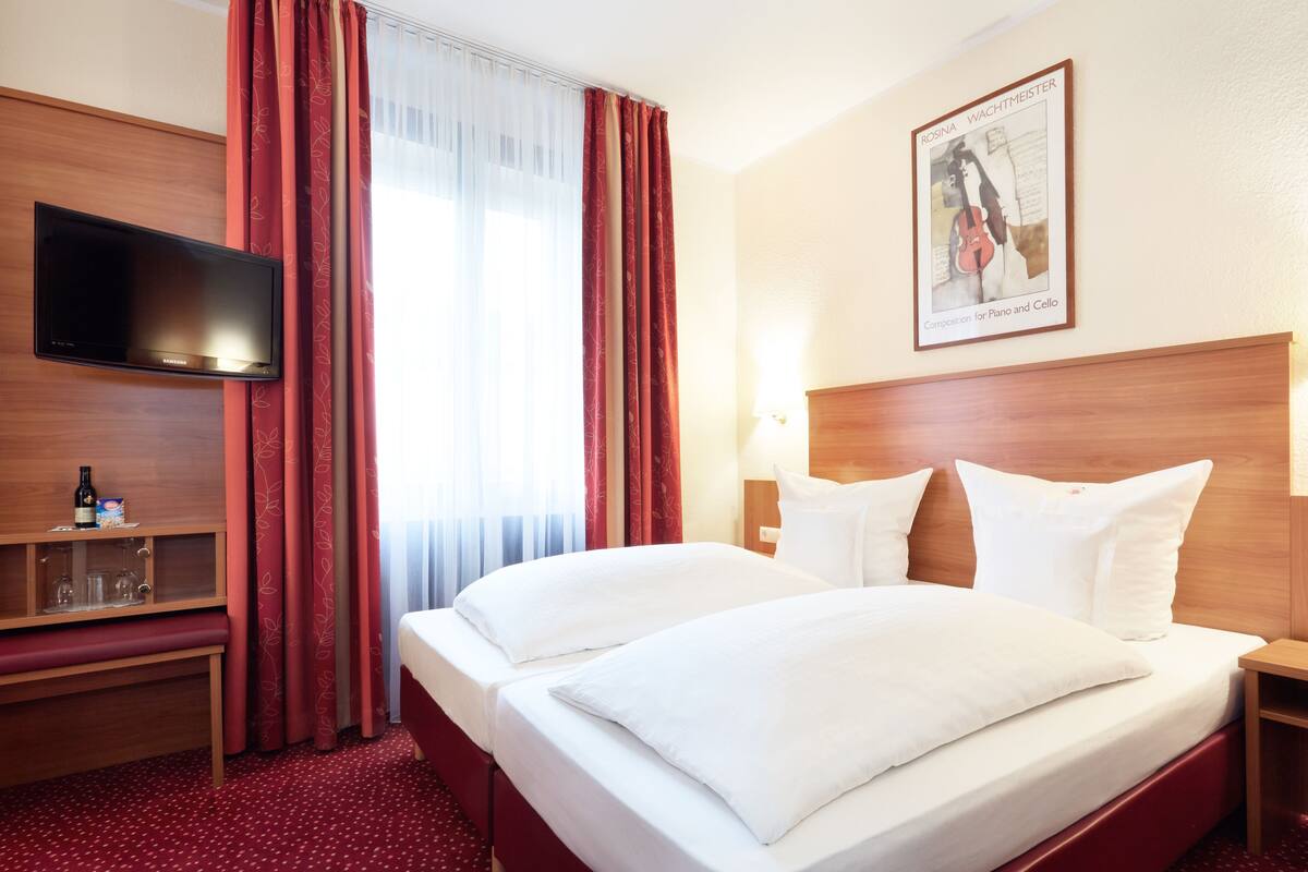 Quarto de hotel com cama, televisão fixada na parede, cabeceira de madeira e um cartaz na parede.