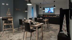 Uma área de refeições moderna com televisão, cadeiras, mesas e bancada de cozinha.