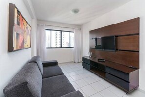 Uma sala de estar moderna com um sofá cinzento, um rack de entretenimento de madeira e uma janela grande com cortinas.