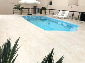 Uma piscina com deck revestido, rodeada por espreguiçadeiras e plantas em vasos.