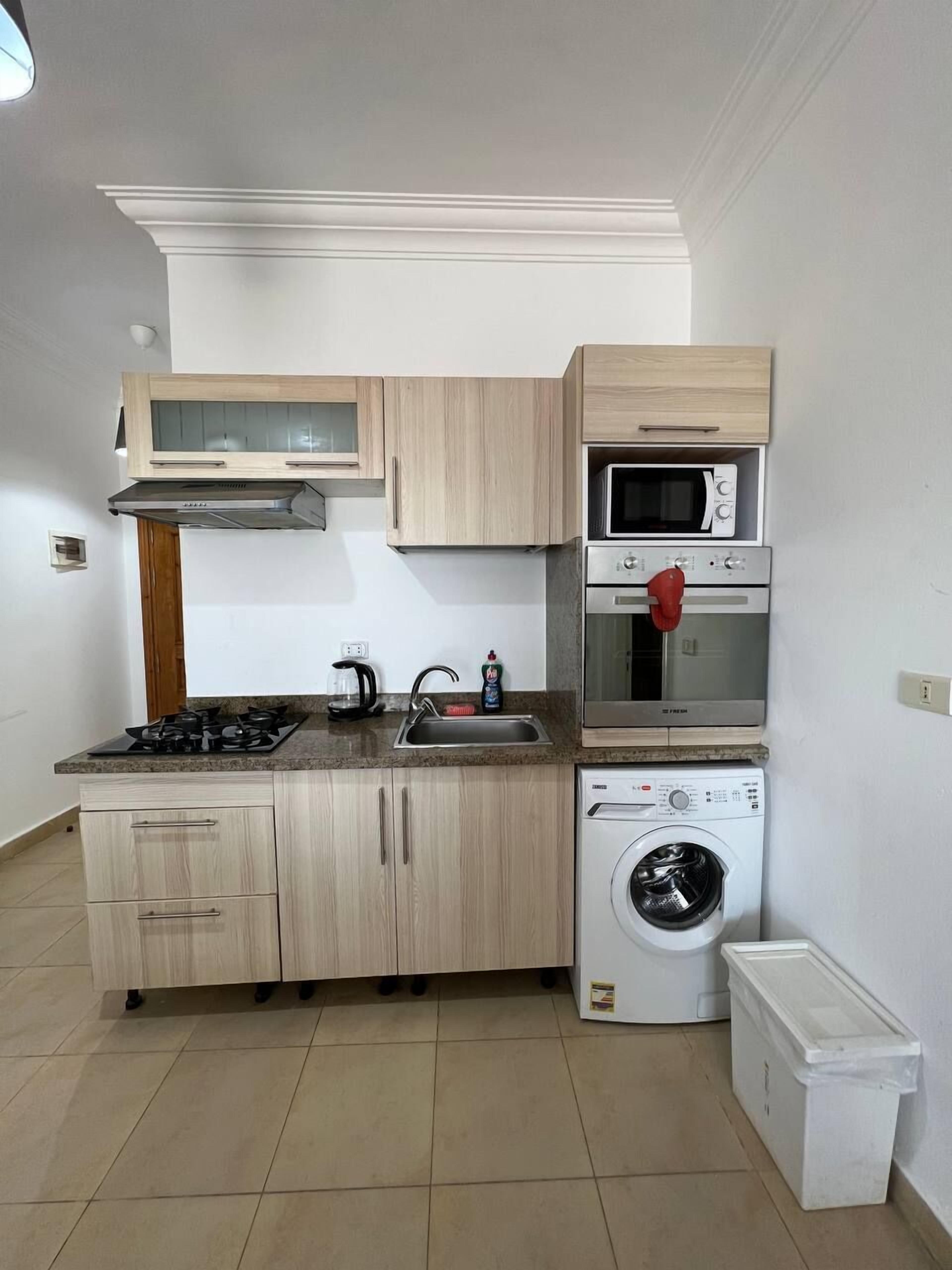 Uma cozinha compacta com fogão a gás, micro-ondas, forno, pia e máquina de lavar embutida.