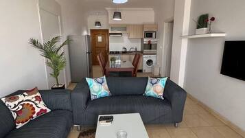 Uma sala de estar moderna com um conjunto de sofás, uma mesa de centro e uma cozinha ao fundo.