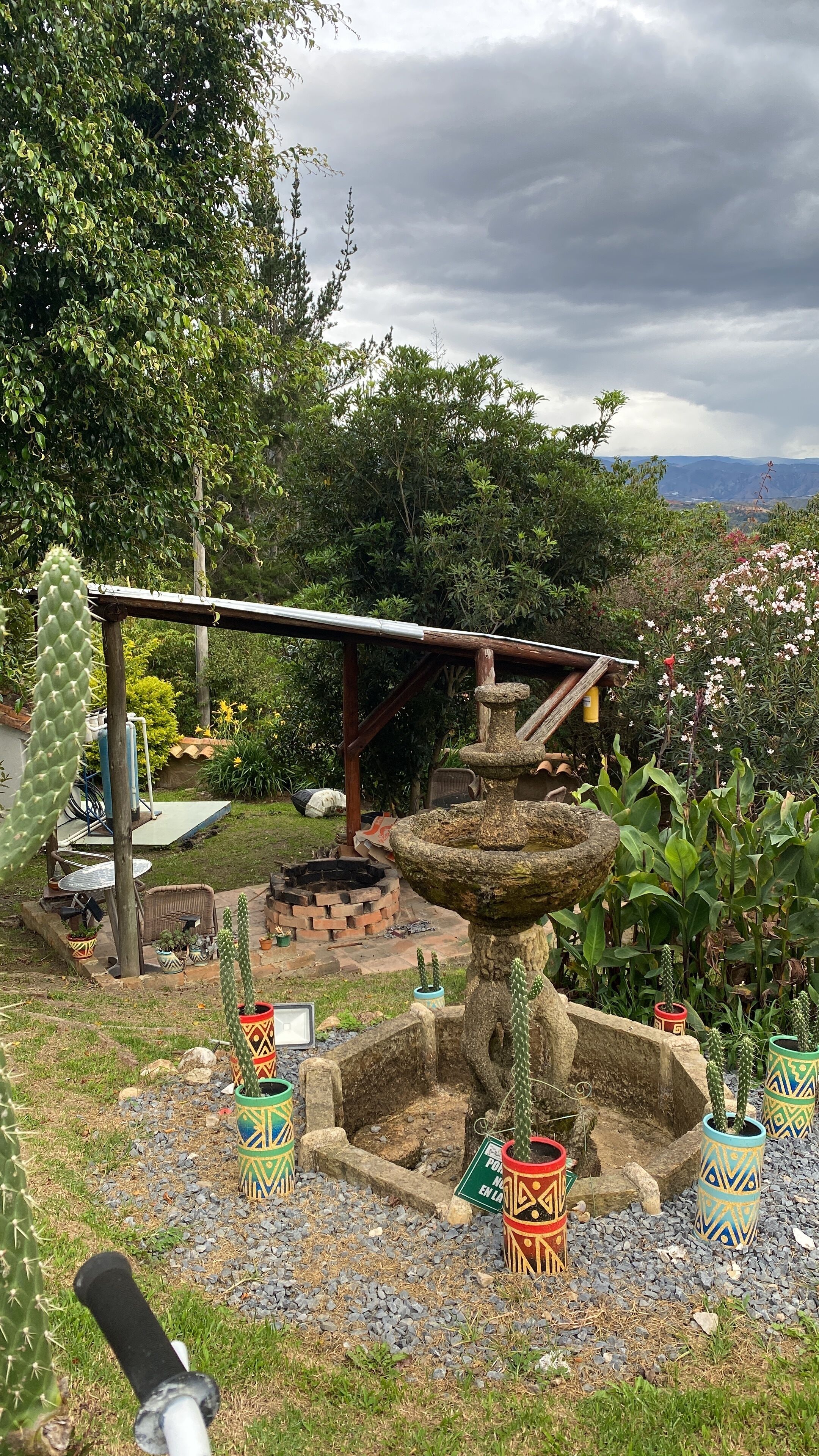 Um jardim com uma fonte de pedra, cactos em vasos e um pergolado.