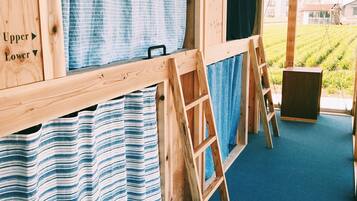 Interior de uma cabana de madeira com carpete azul, cortinas listradas e vista para um campo verde lá fora.