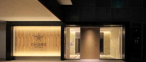 Exterior do Candeo Hotels, com fachada moderna, ampla entrada de vidro e sinalização iluminada.