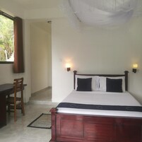 Quarto com cama de madeira, duas luminárias de cabeceira, uma escrivaninha com cadeira e uma janela com cortinas.