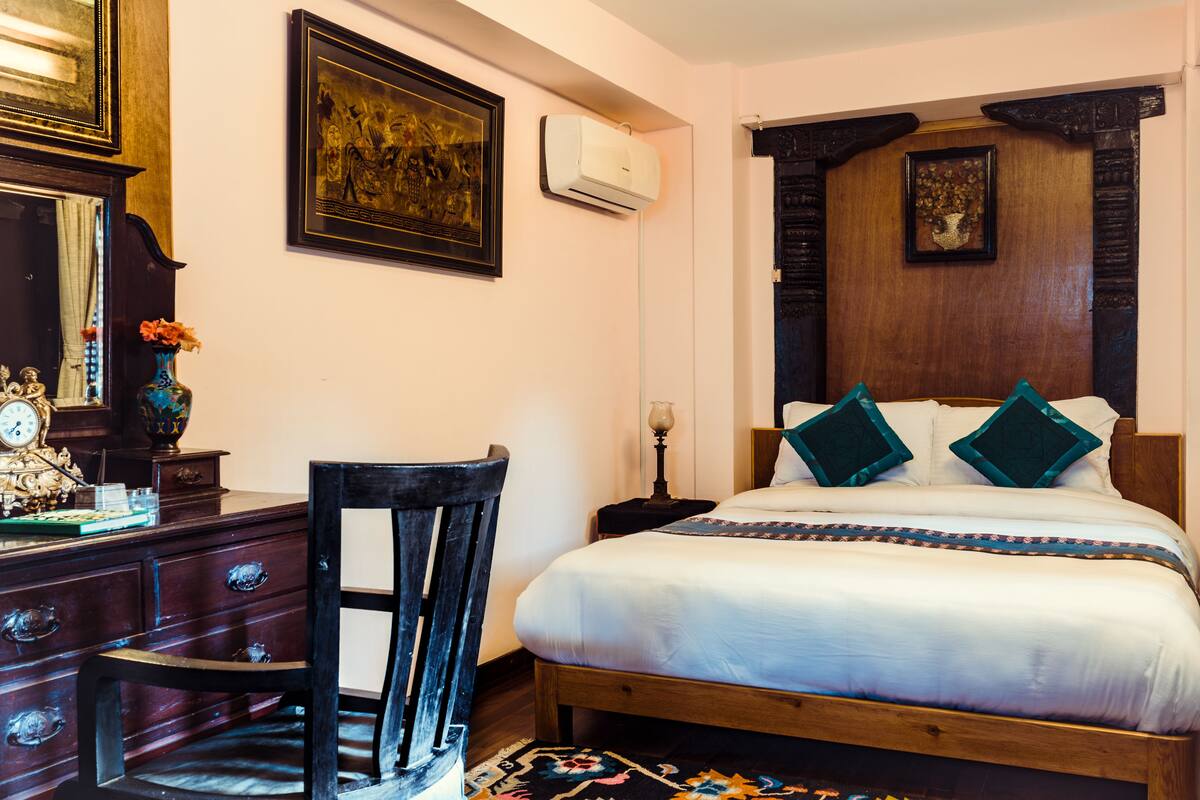 Um quarto com cama de madeira, mesa de cabeceira, cadeira, cômoda e espelho.