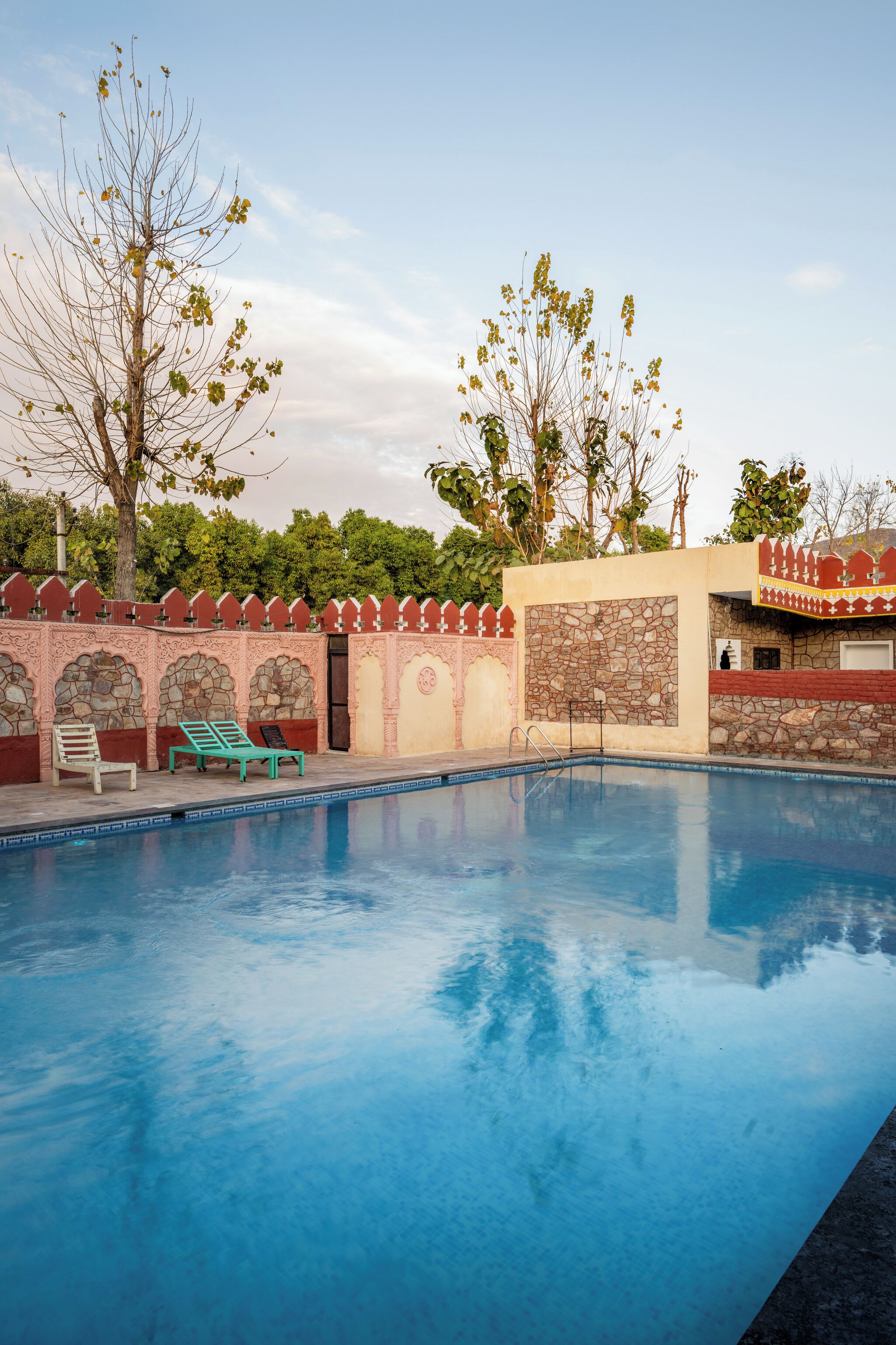 Piscina com muro de pedra e um pequeno edifício com porta.
