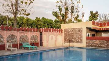 Piscina com muro de pedra e um pequeno edifício com porta.