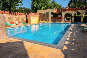Piscina com muro de pedra e arcos, cercada por espreguiçadeiras e um deck ladrilhado.