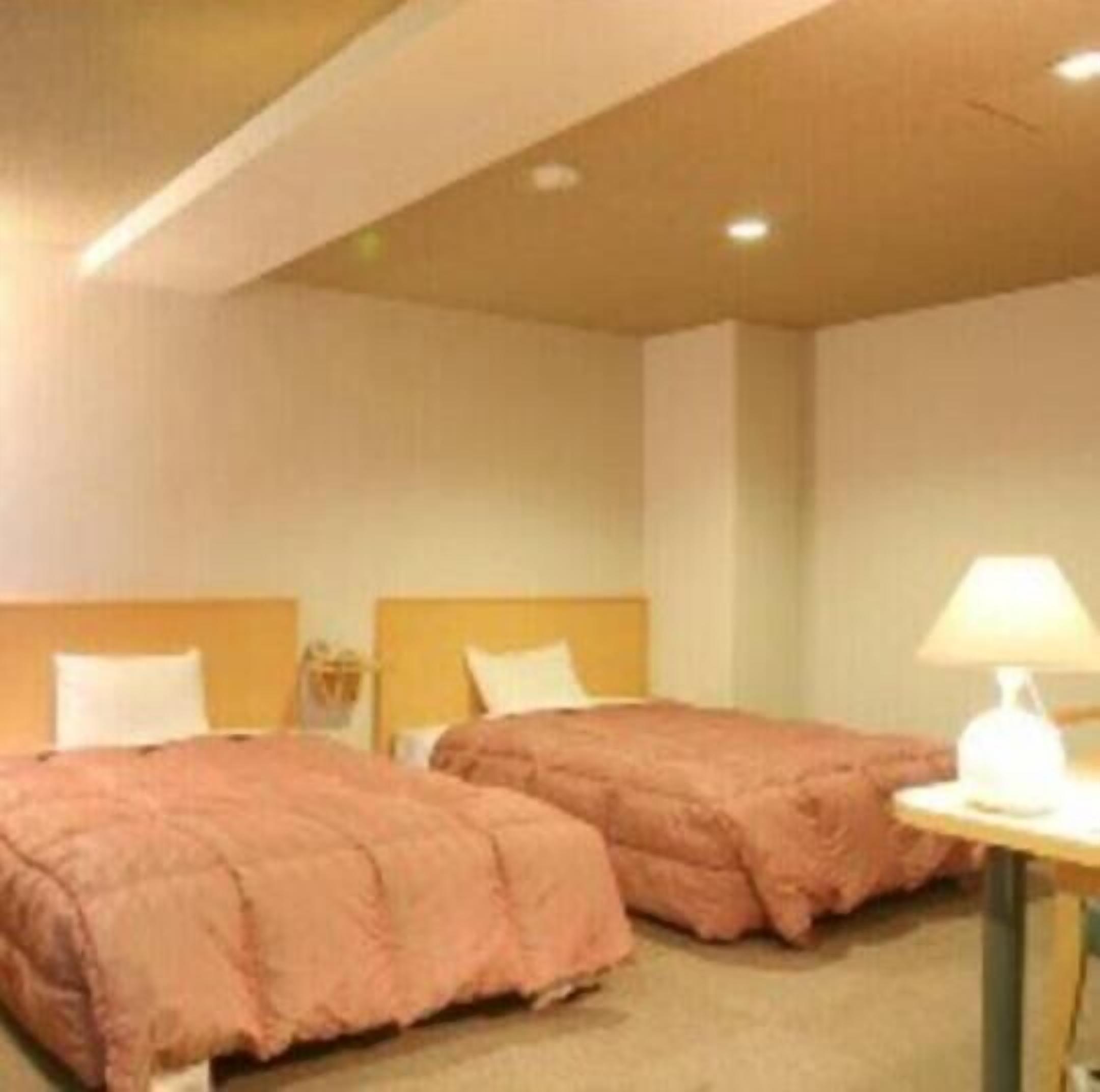 Quarto de hotel com duas camas, uma mesa de cabeceira com abajur e cabeceira.
