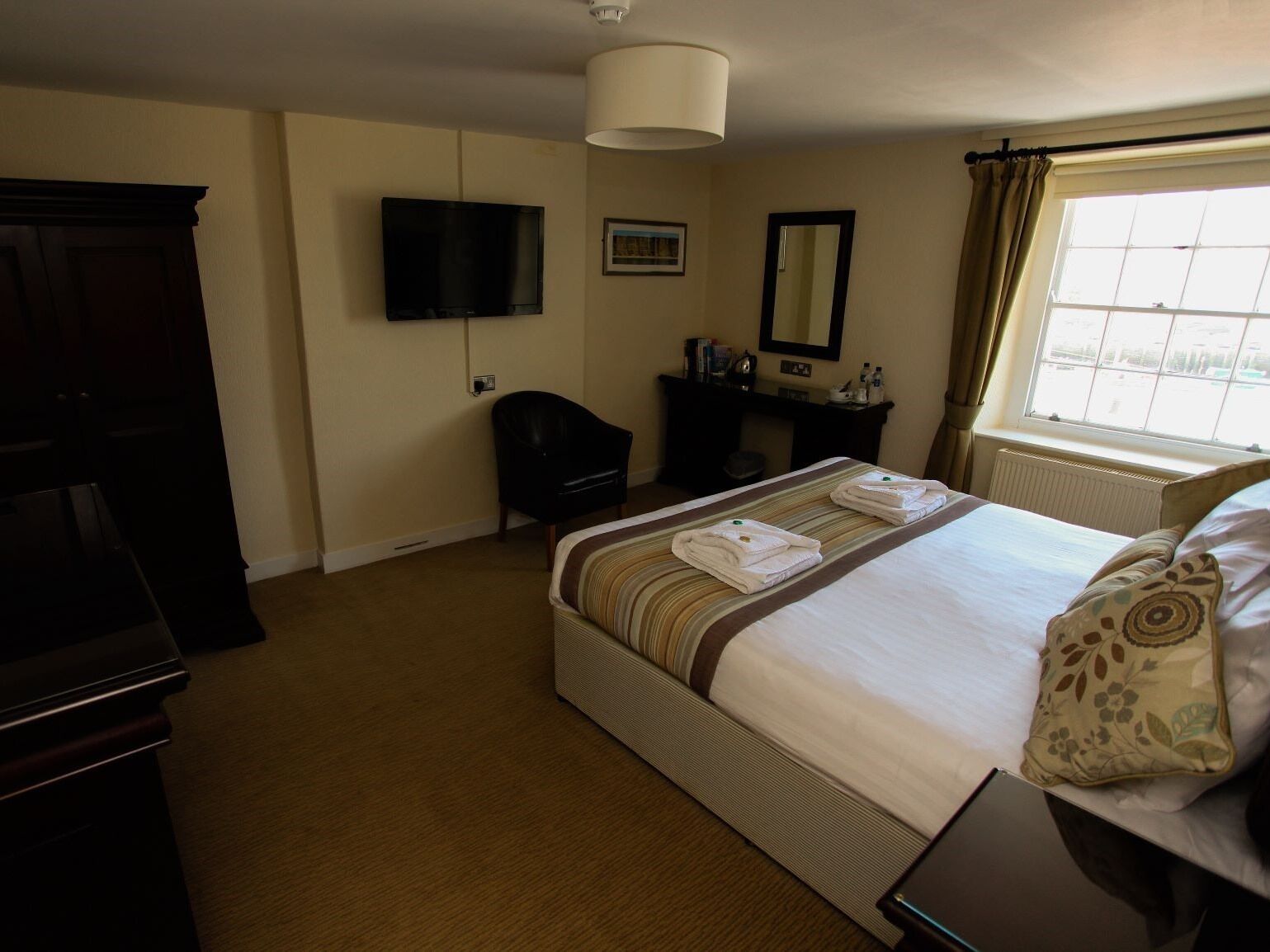 Quarto de hotel com cama, televisão, escrivaninha, cadeira e janela com cortinas.