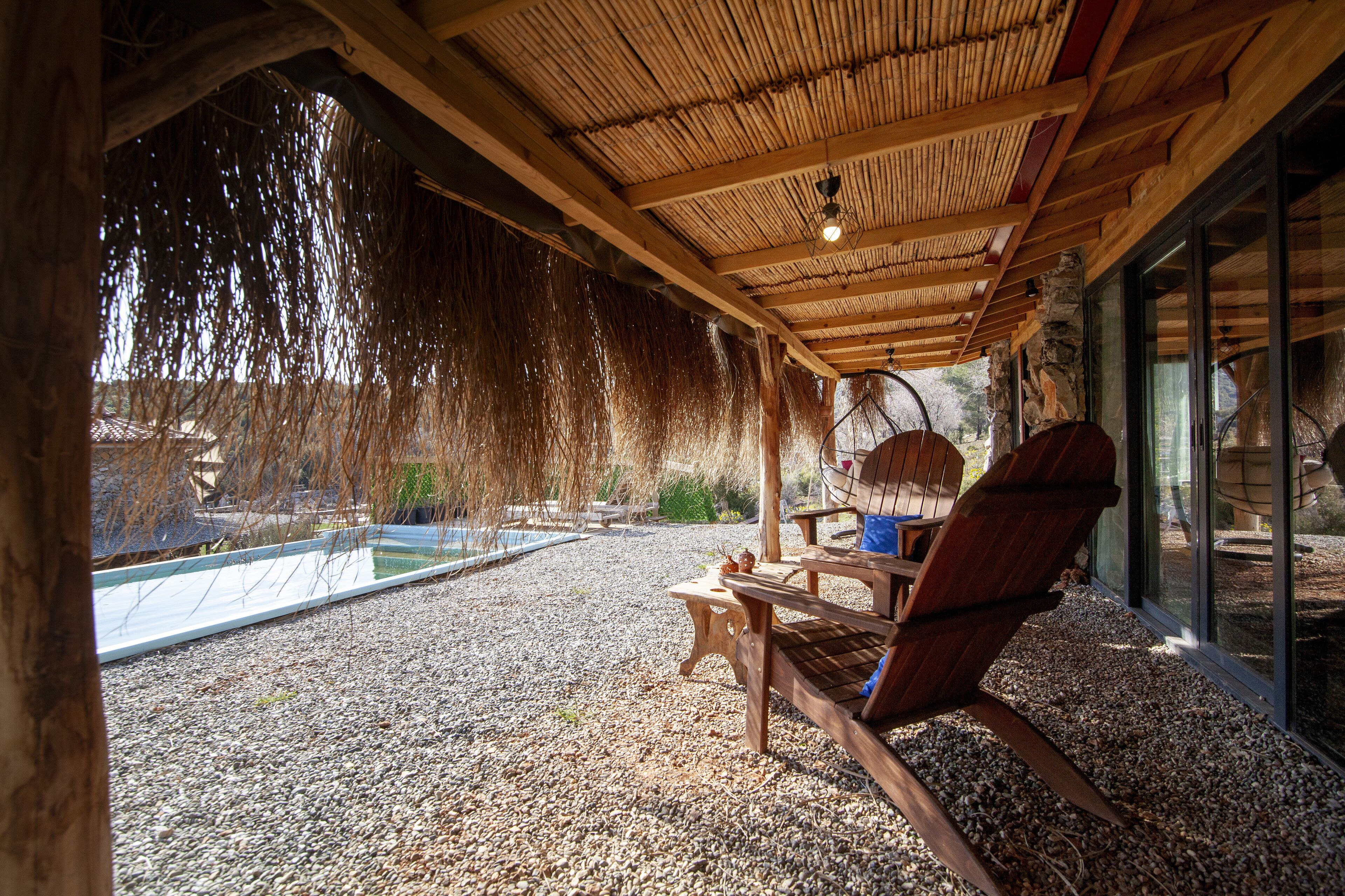 Uma área externa coberta com piscina, móveis de madeira e um muro de pedra.