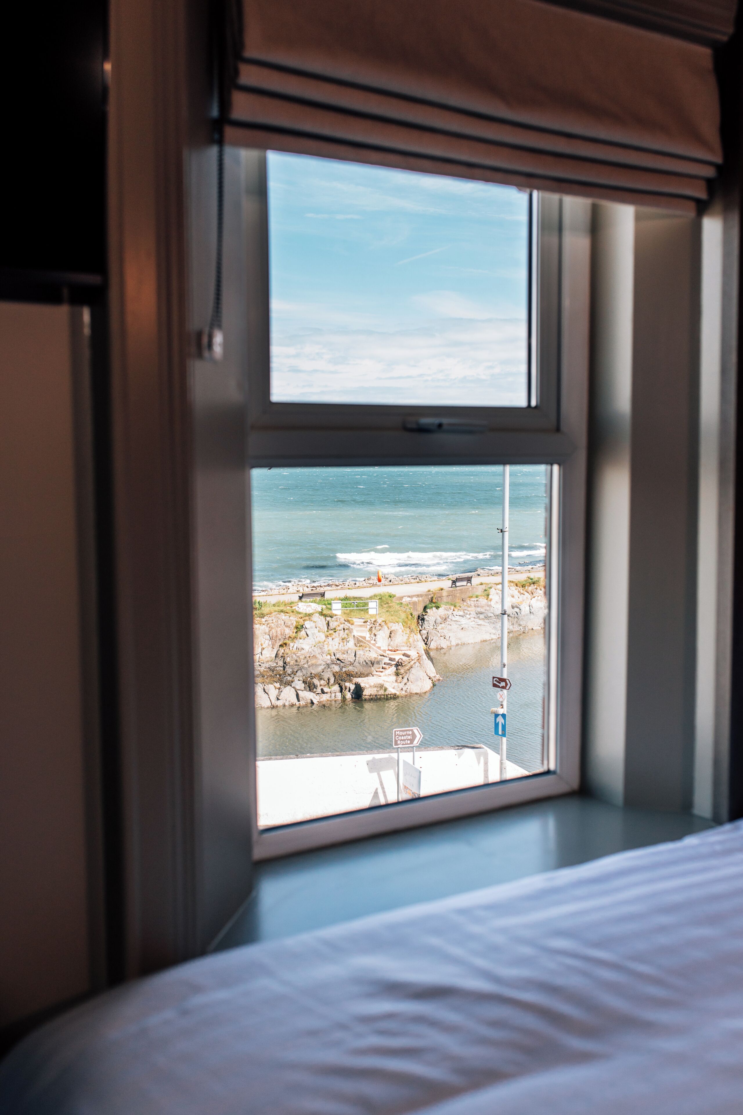 Janela com vista para uma costa rochosa e águas calmas.