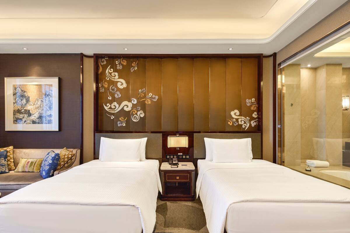 Quarto de hotel com duas camas, uma mesa de cabeceira, um abajur e um espelho grande.