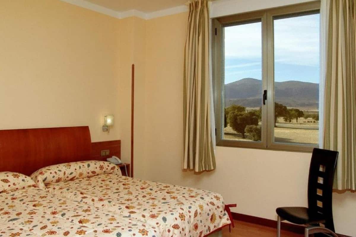 Quarto de hotel com cama, cadeira, janela com cortinas e vista para a paisagem.