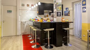 Cozinha moderna com ilha preta, painel de azulejos branco e banquetas. Há diversos eletrodomésticos e um tapete vermelho que leva à área do bar.