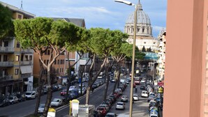 Vista da rua com carros estacionados, árvores e um grande edifício com cúpula ao fundo.