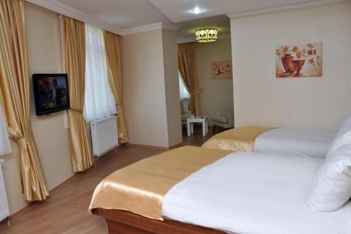 Quarto de hotel com cama de casal, uma pequena escrivaninha, uma cadeira e um quadro na parede.