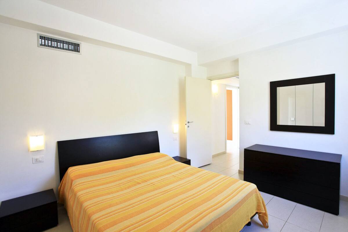 Quarto de hotel com uma cama, mesas de cabeceira, cómoda e espelho na parede.