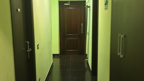 Corredor com paredes verdes, piso de azulejos escuros e portas em ambos os lados.