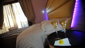 Quarto de hotel com uma cama, dois copos de champanhe sobre uma mesa e uma flor sobre um guardanapo.