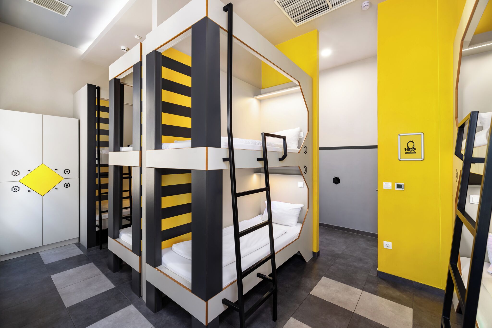 Quarto com beliche, um guarda-roupa e parede amarela com um logotipo.